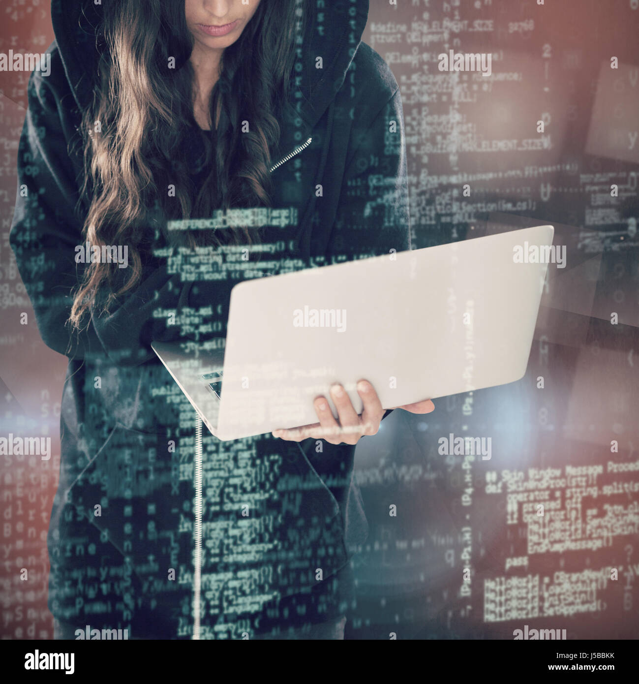 Female hacker in black hoodie using laptop against abstract black room ...