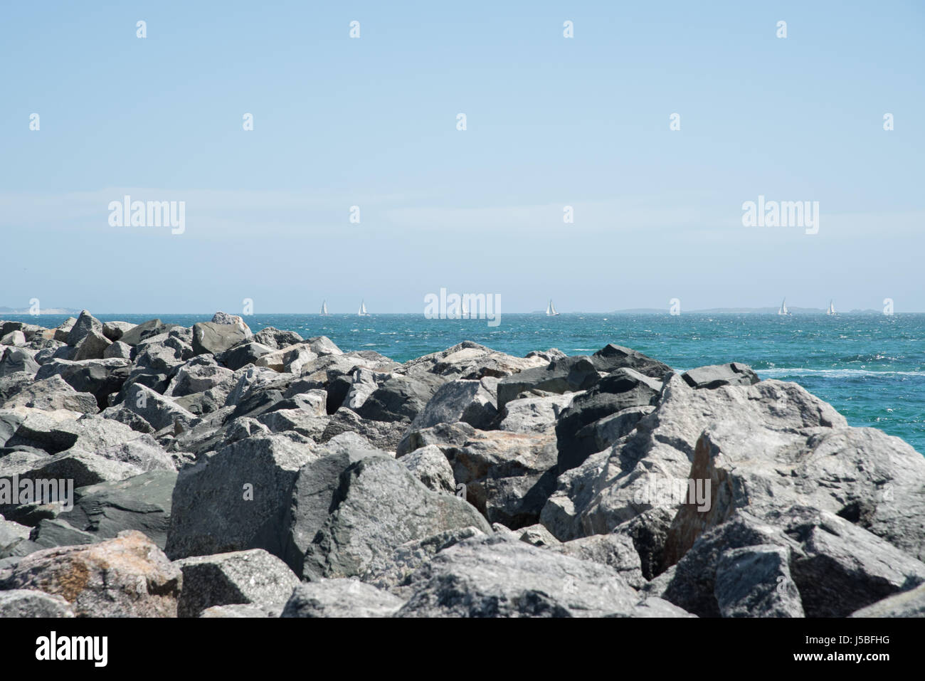 Rocky groyne along the Indian Ocean coastline under a clear blue sky in ...