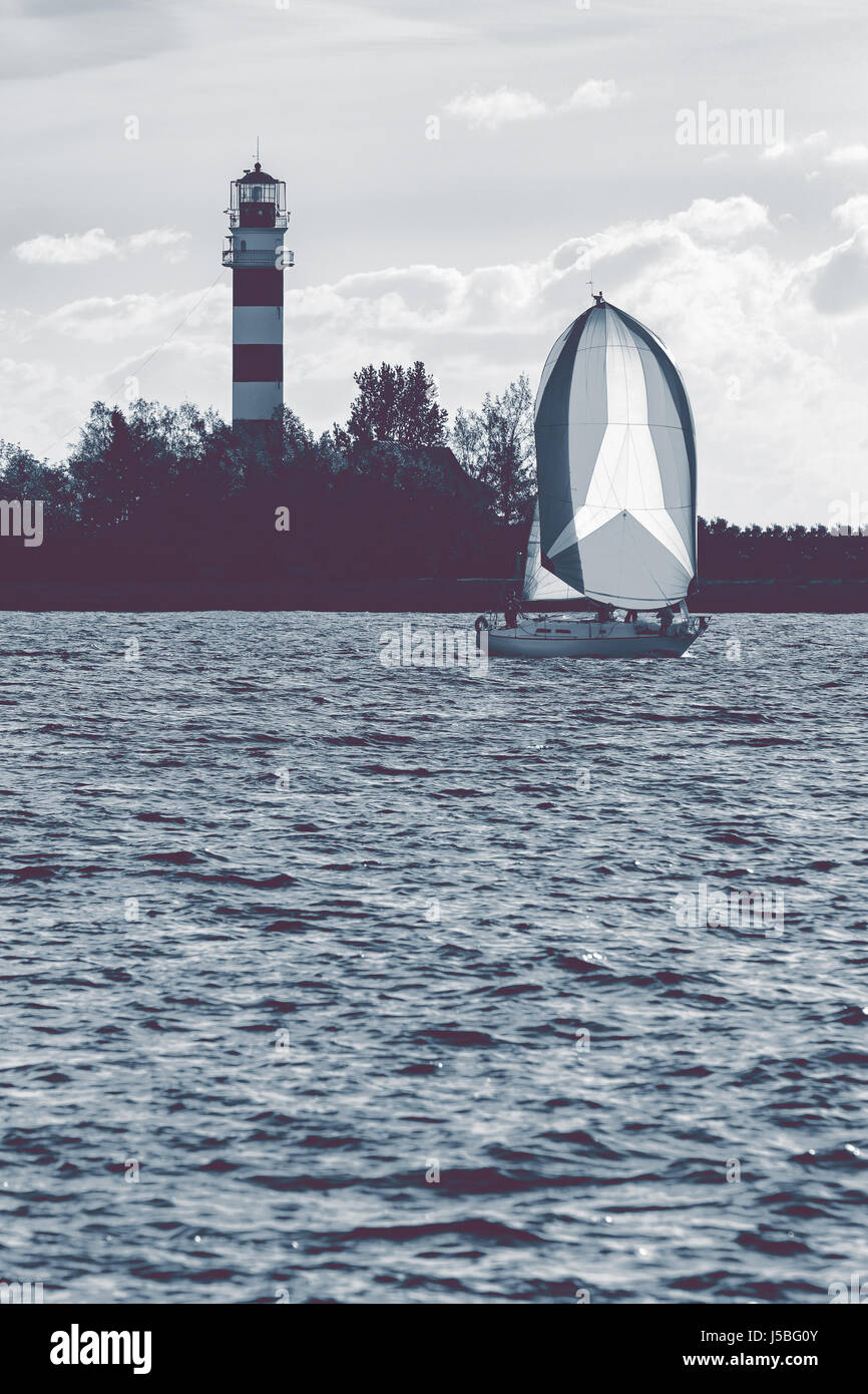 Sailboat sailing past the big lighthouse in evening, Latvia Stock Photo ...
