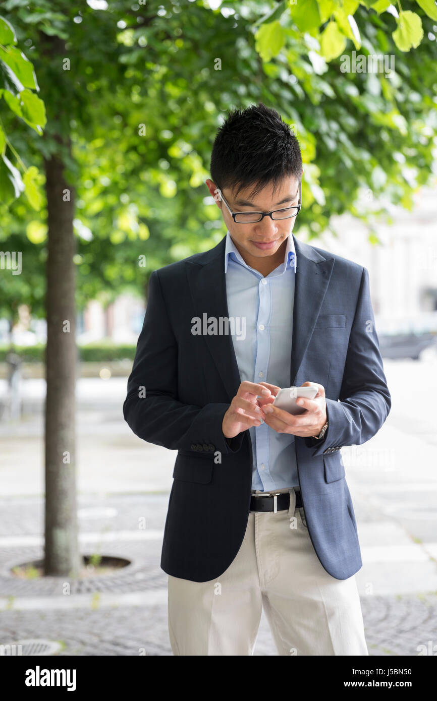 Chinese business Man using his Smart phone outdoors in modern city ...