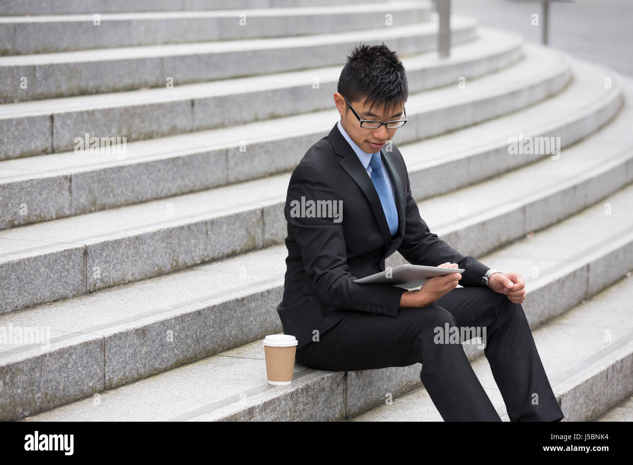 High angle view of a Chinese man sitting on steps using a tablet device ...