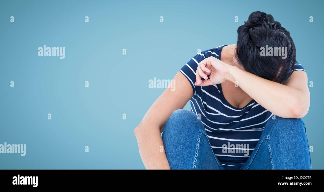 Digital composite of Woman sitting and crying into arm against blue ...