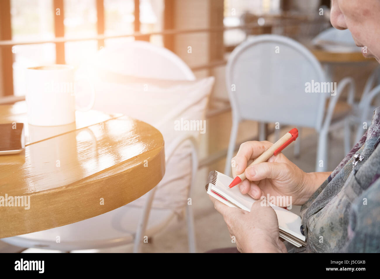 thoughtful old elderly senior woman writing notes in cafe coffee shop ...