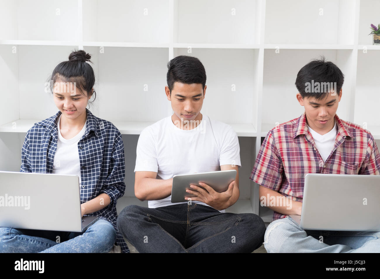 young asian people are using different gadgets and smiling, sitting ...