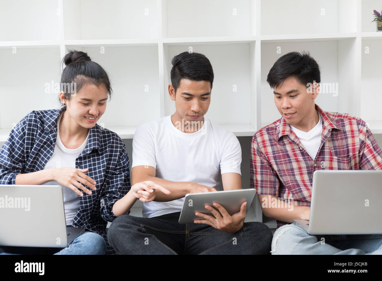 young asian people are using different gadgets and smiling, sitting ...
