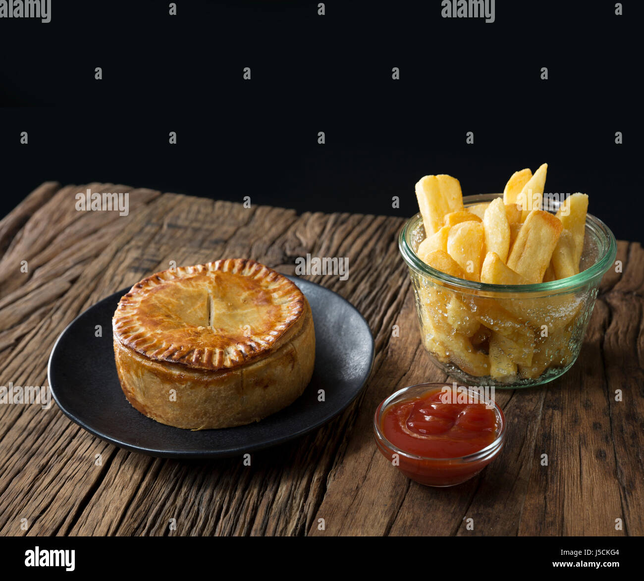 A Traditional British meat pie and chips sitting on a rustic wooden ...