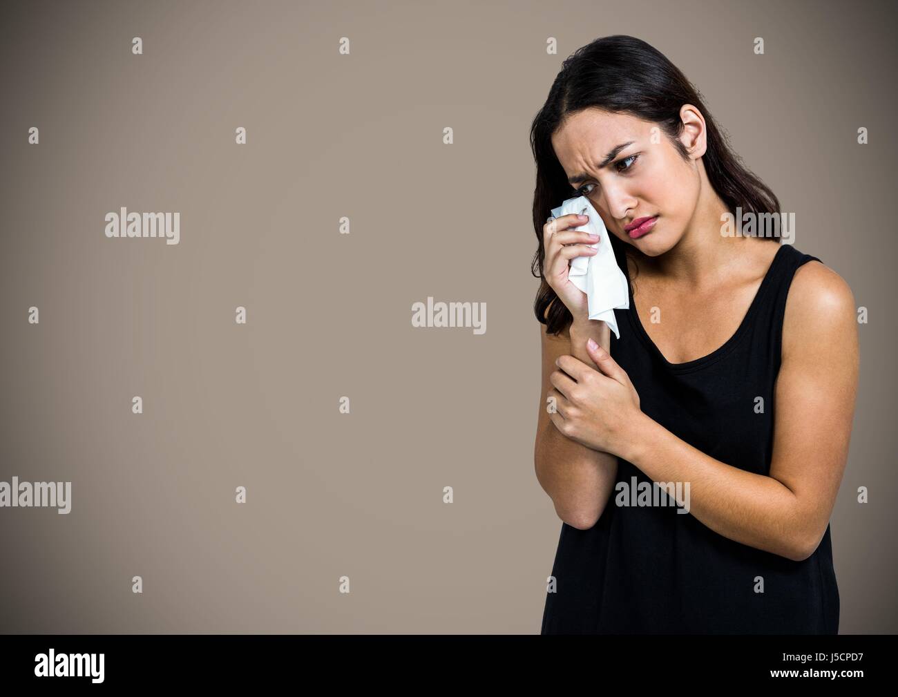 Digital composite of Woman crying into tissue against brown background ...