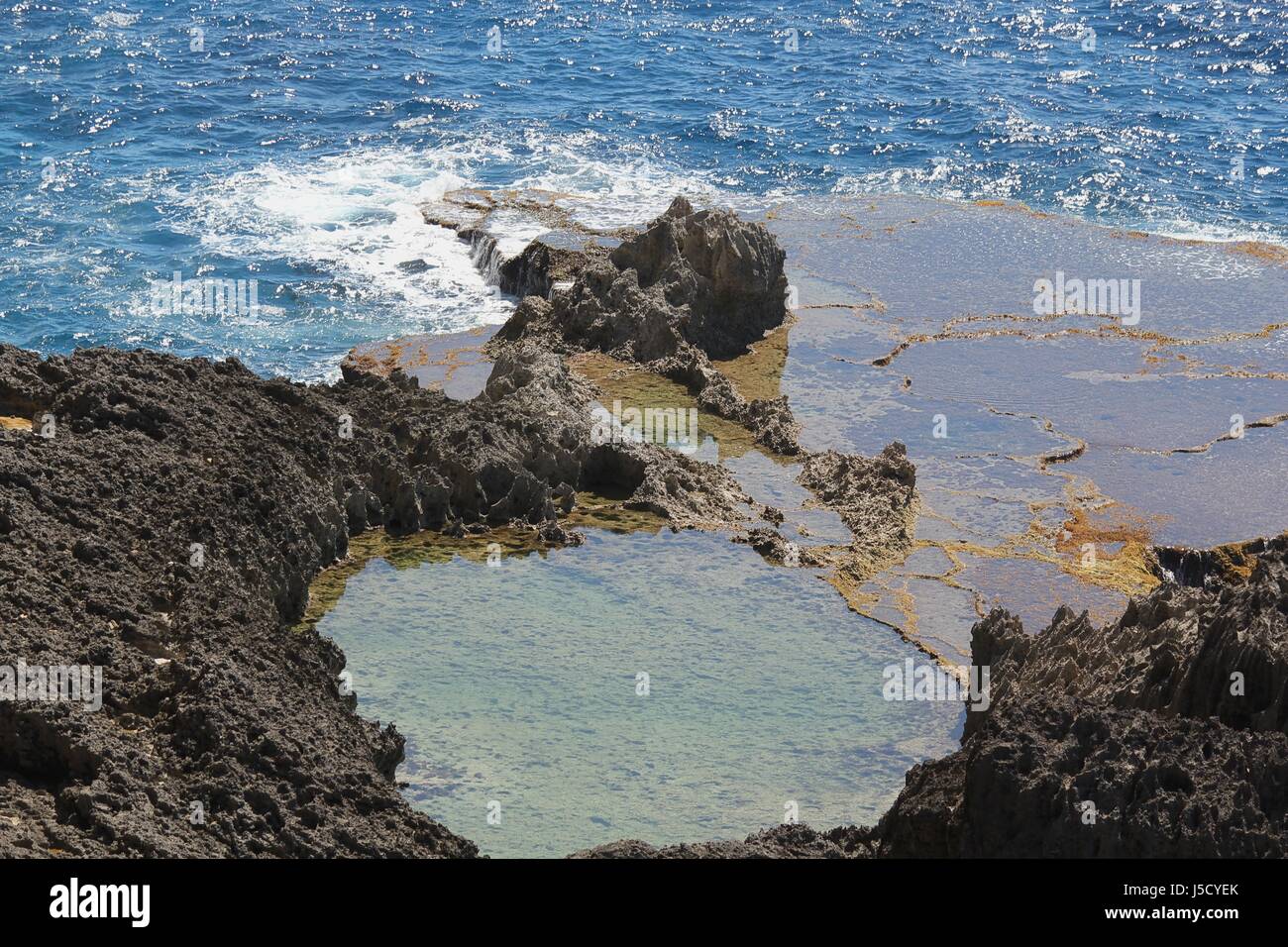 A small pool forms in a rocky pool at the foot of the cliffs Stock ...
