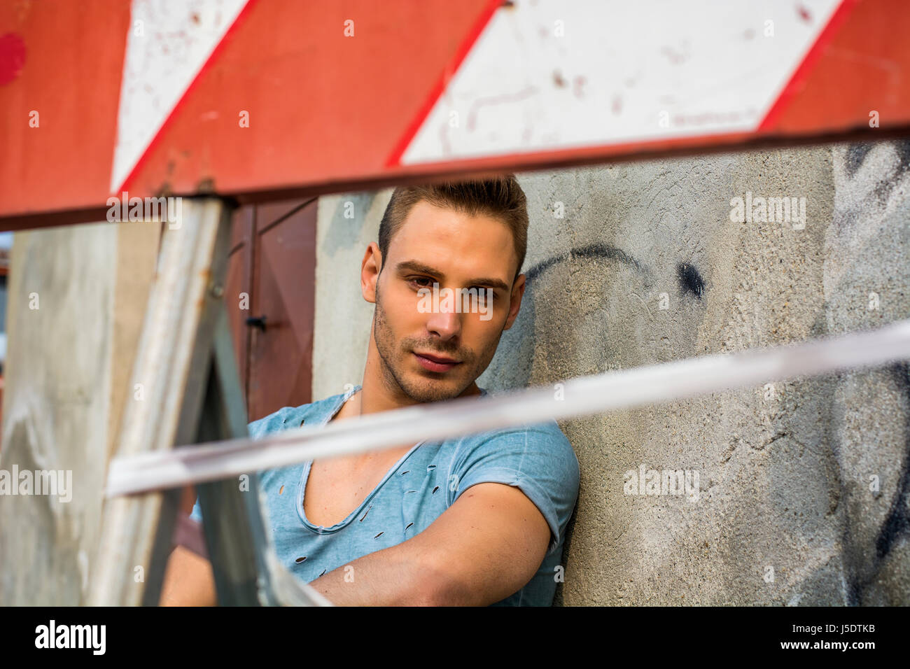 Handsome young man sitting against concrete wall behind barrier Stock ...