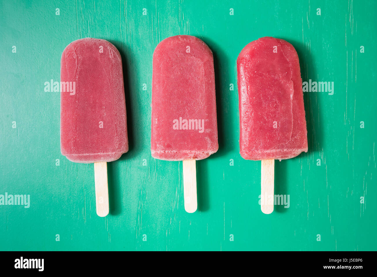 Three Homemade Raspberry and vanilla ice pops on a green wooden ...