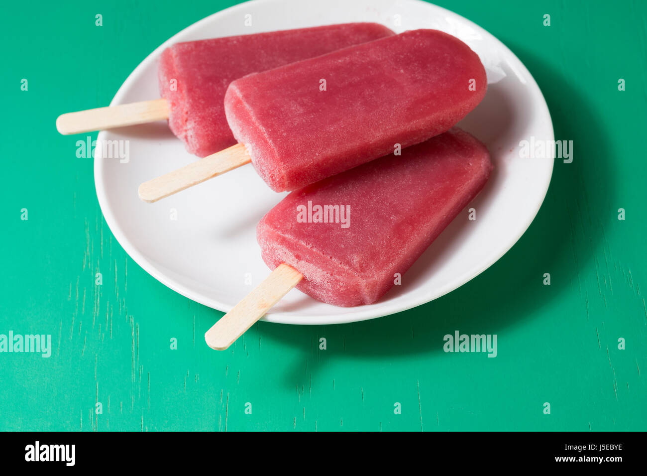 3 Homemade Raspberry and vanilla ice pops on a green wooden background ...