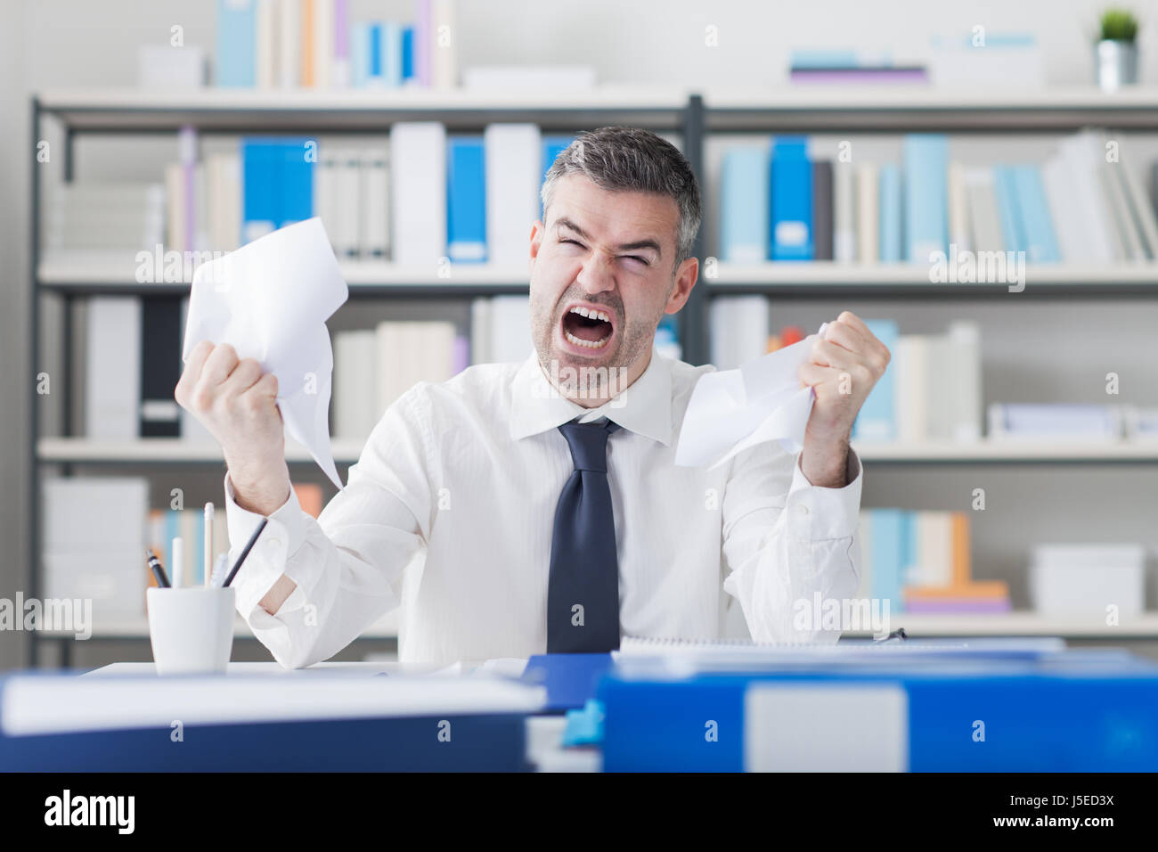 Angry nervous businessman working at office desk overloaded with ...