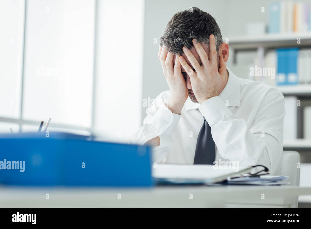 Stressed exhausted man working at office desk with head in hands, he is ...