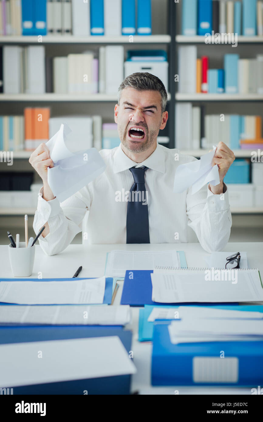 Angry nervous businessman working at office desk overloaded with ...