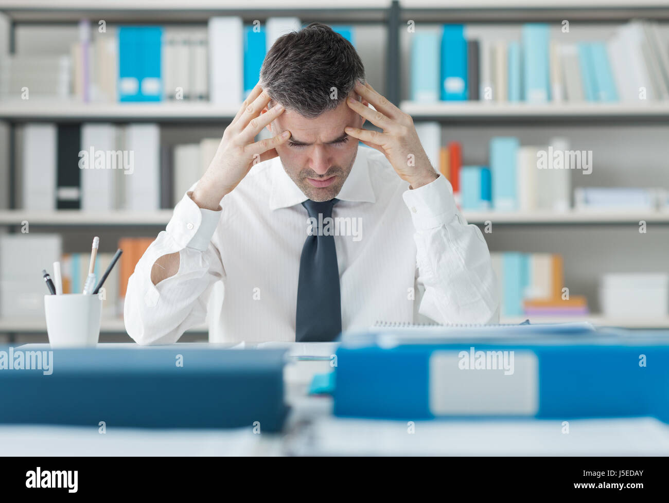 Stressed exhausted man working at office desk with head in hands, he is ...