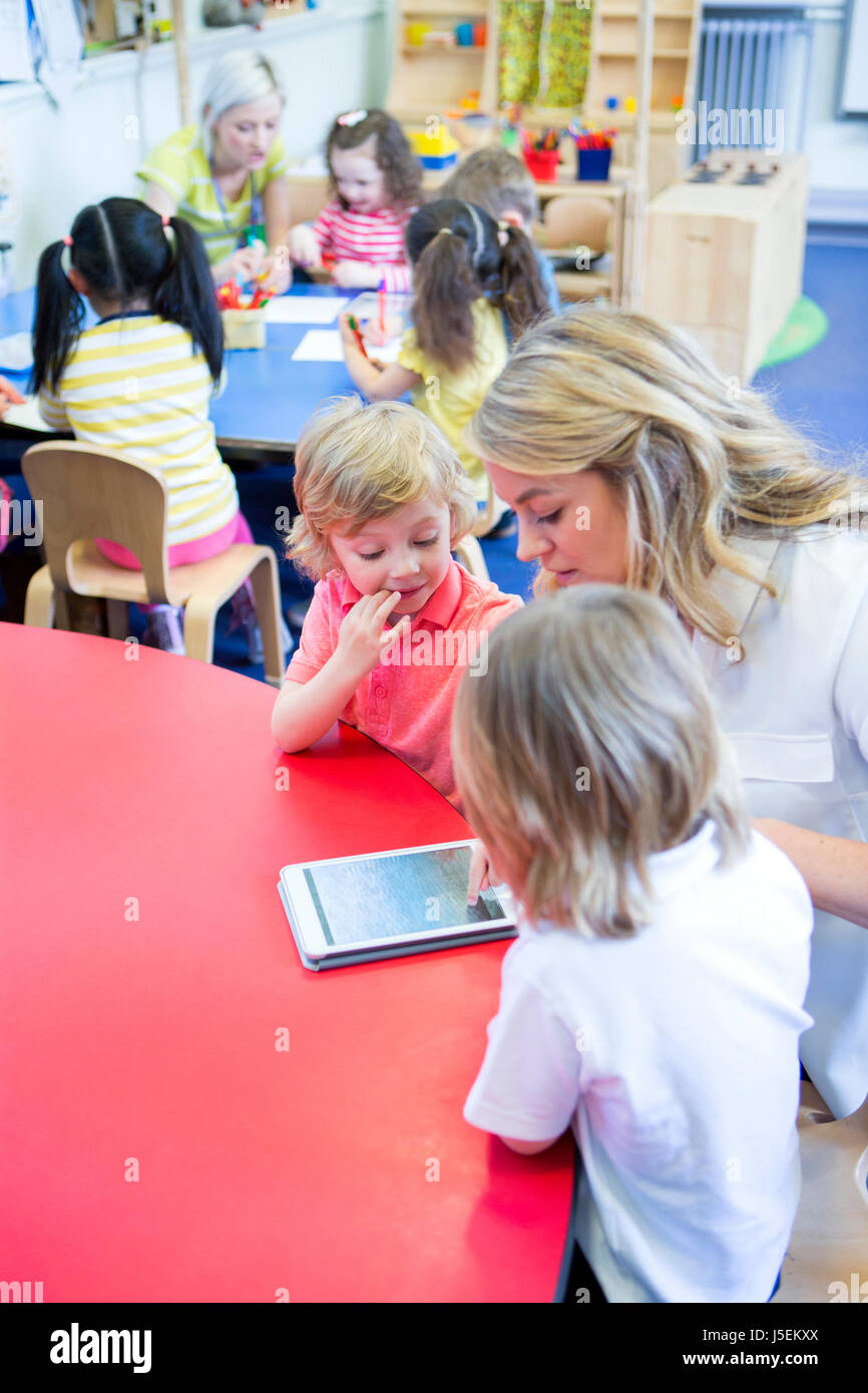 Female teacher using a digital tablet with her nursery students in a ...