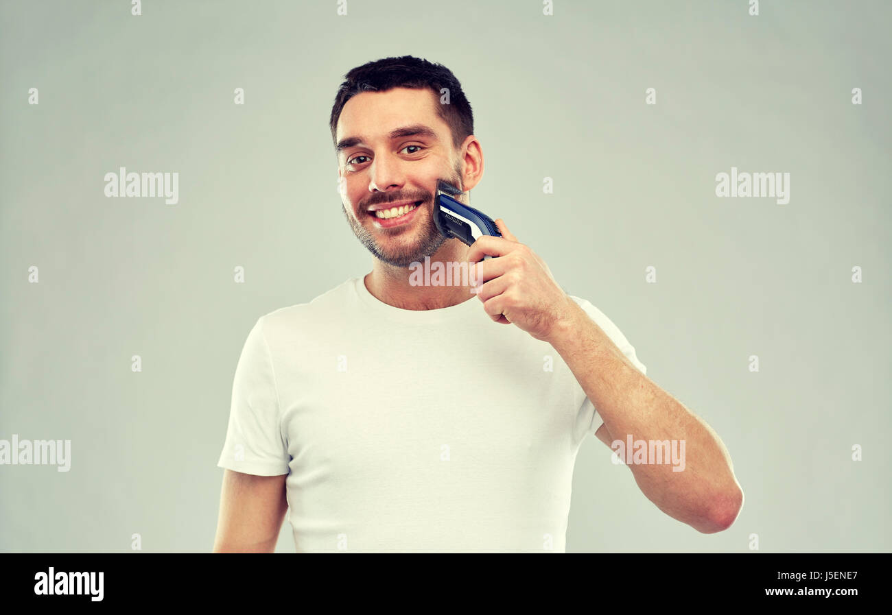 smiling man shaving beard with trimmer over gray Stock Photo - Alamy