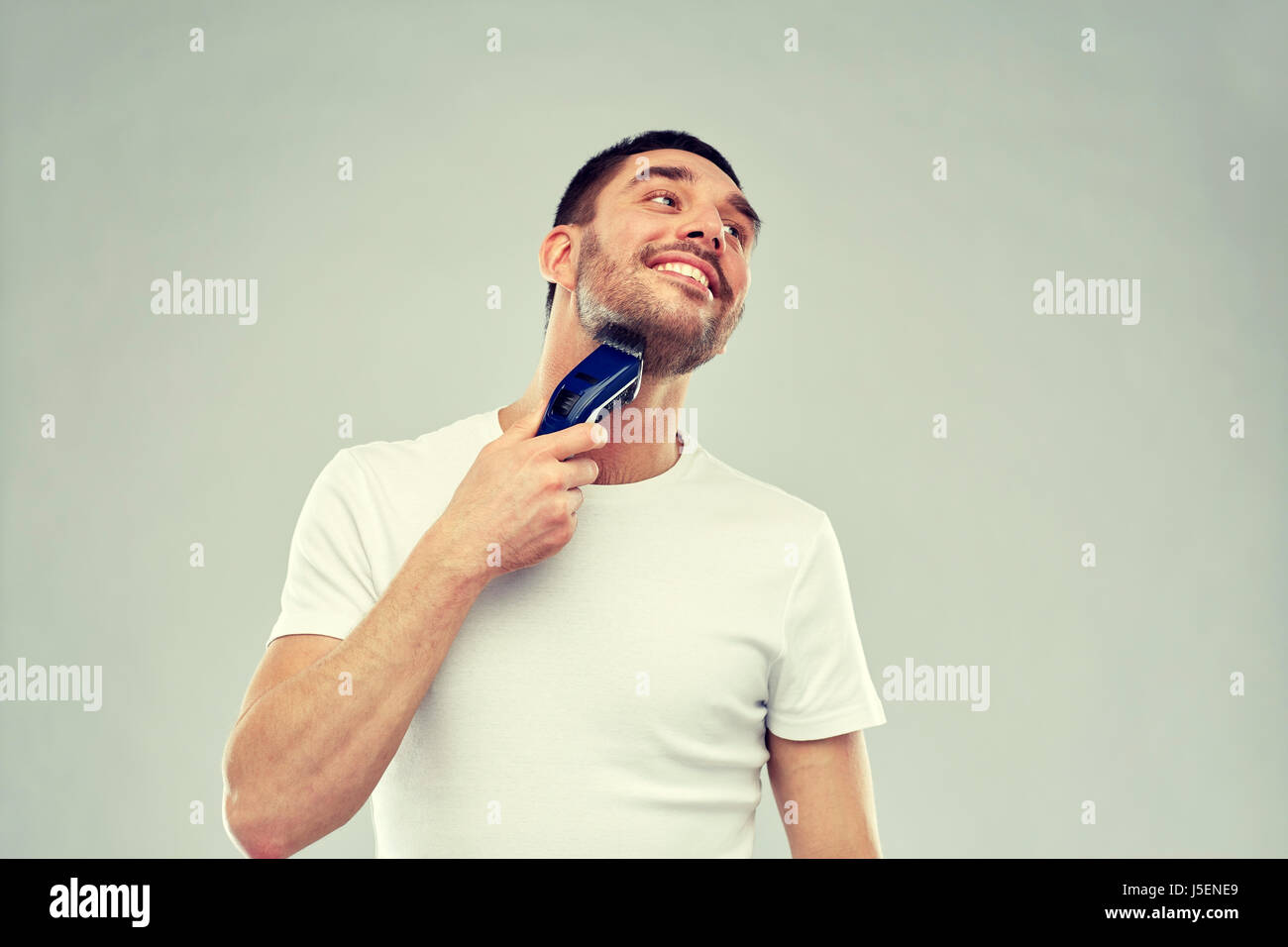 smiling man shaving beard with trimmer over gray Stock Photo - Alamy