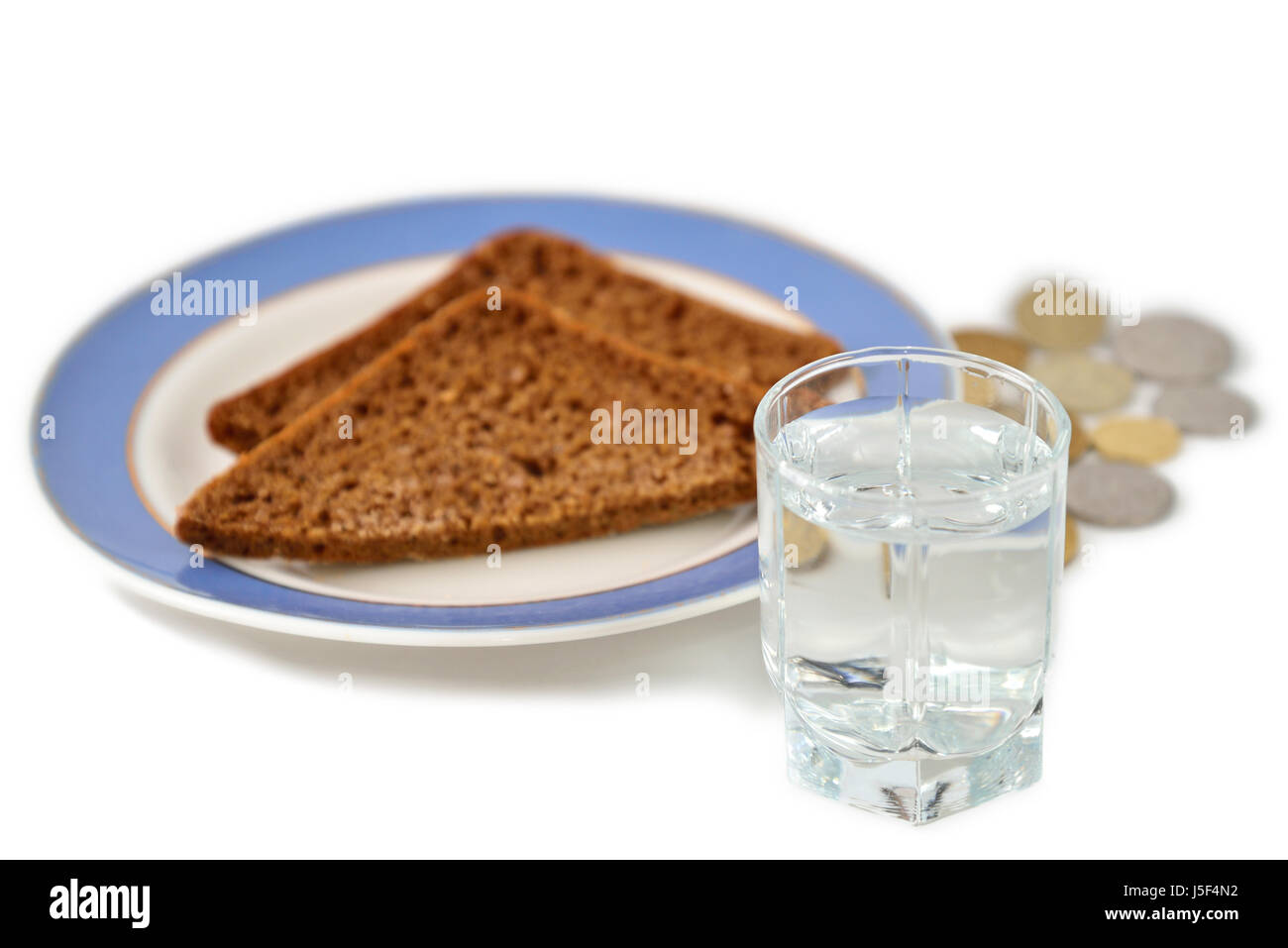 A shot of vodka in the background of a piece of bread and metal coins ...