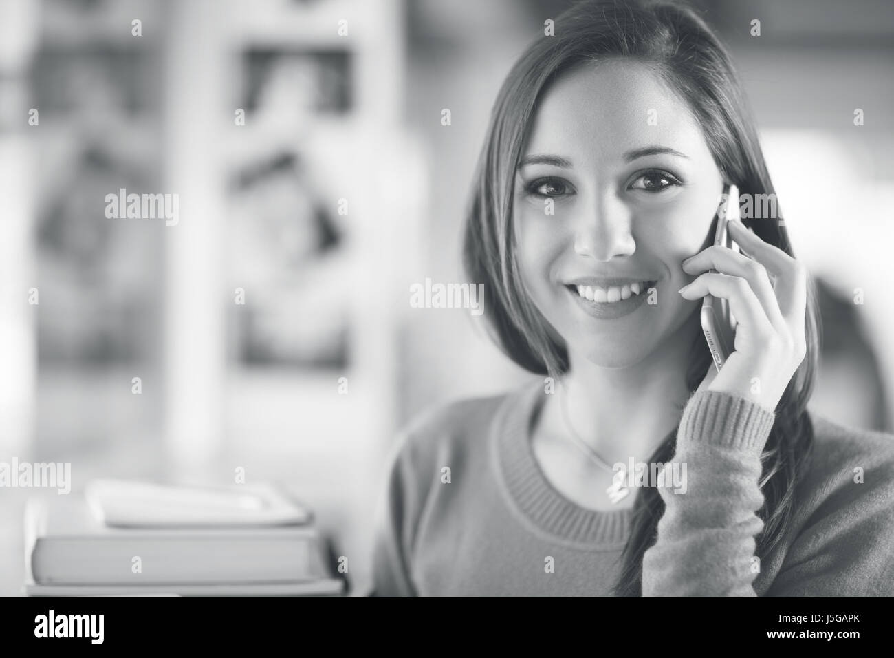 Cute young student girl having a phone call with books on background ...