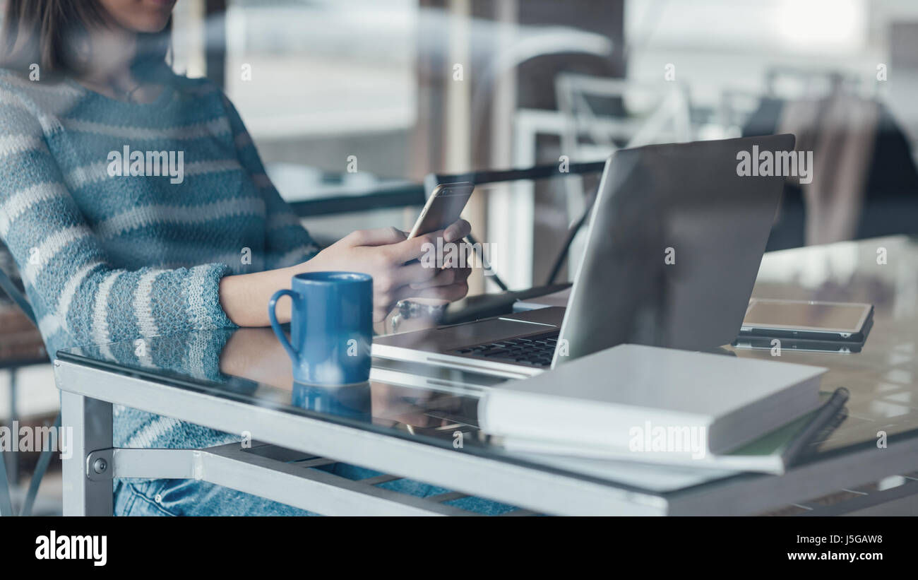 Businesswoman working at office desk and texting with her mobile phone ...