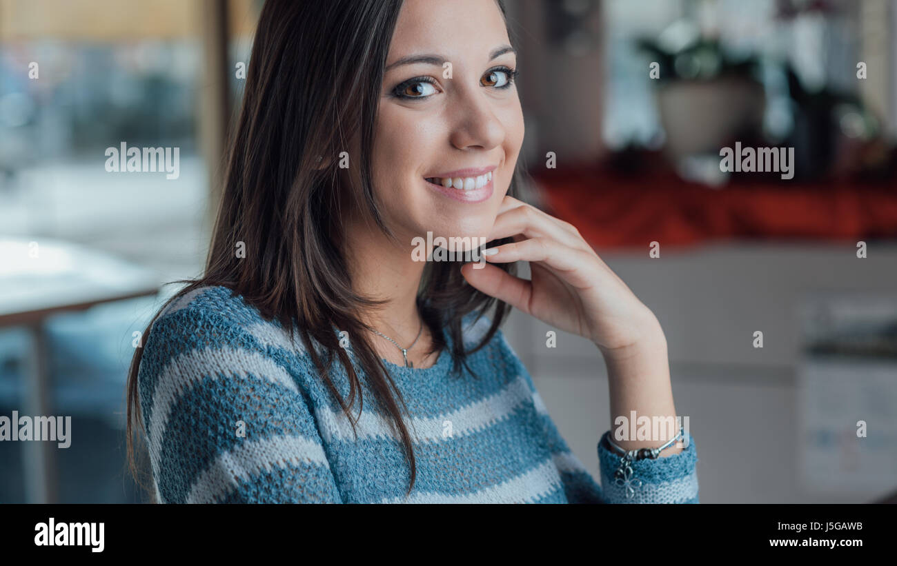 Friendly young woman posing and smiling at camera with bar interior on ...