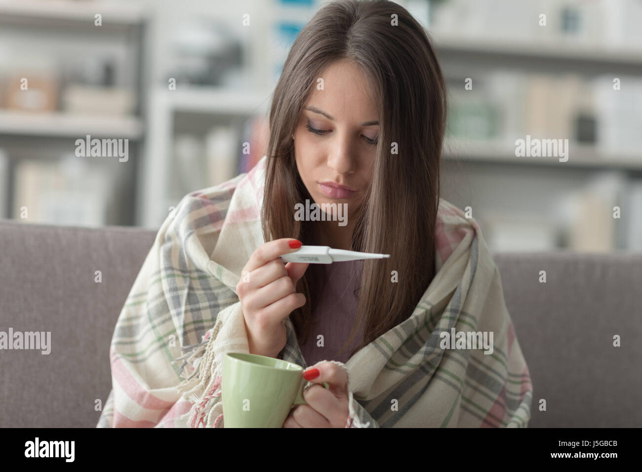 Sick young woman at home on the sofa, she is covering with a blanket ...