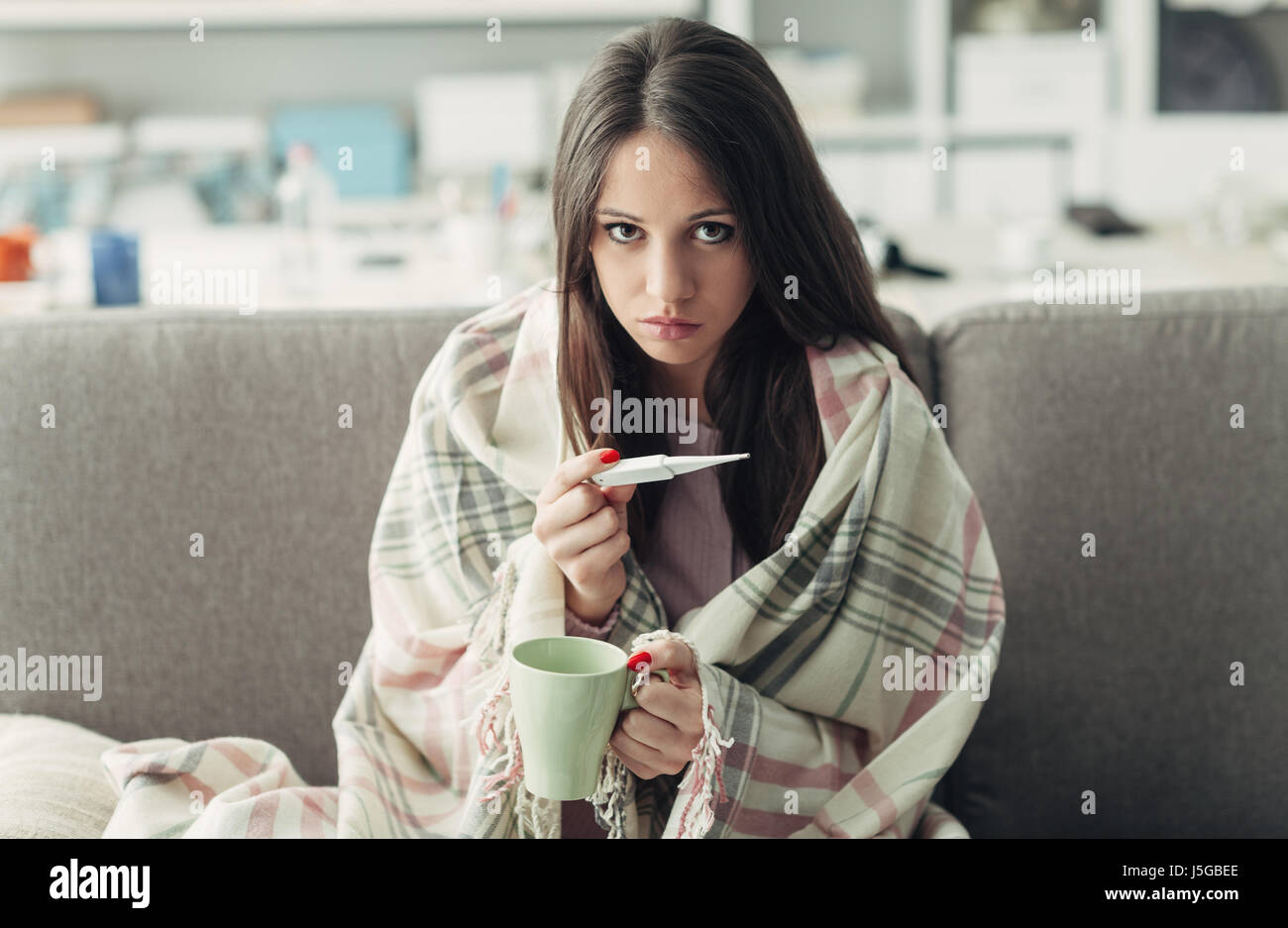 Sick young woman at home on the sofa, she is covering with a blanket ...