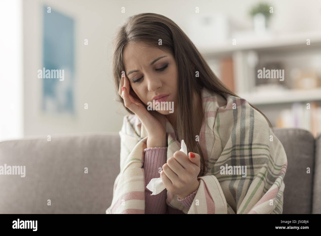 Sick young woman at home on the sofa with cold and headache, she is ...