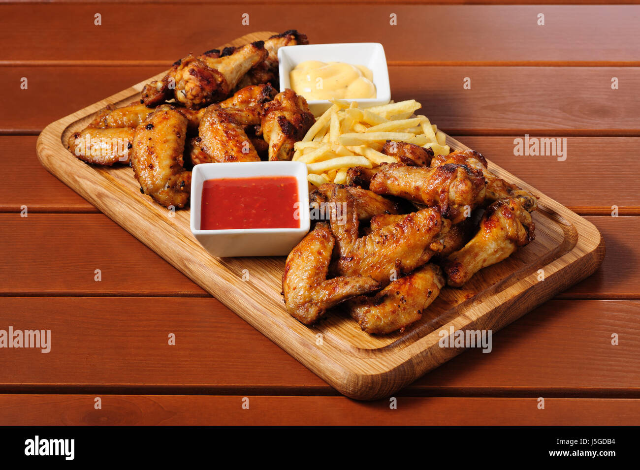 big wooden board with grilled chicken wings with french fries and two ...