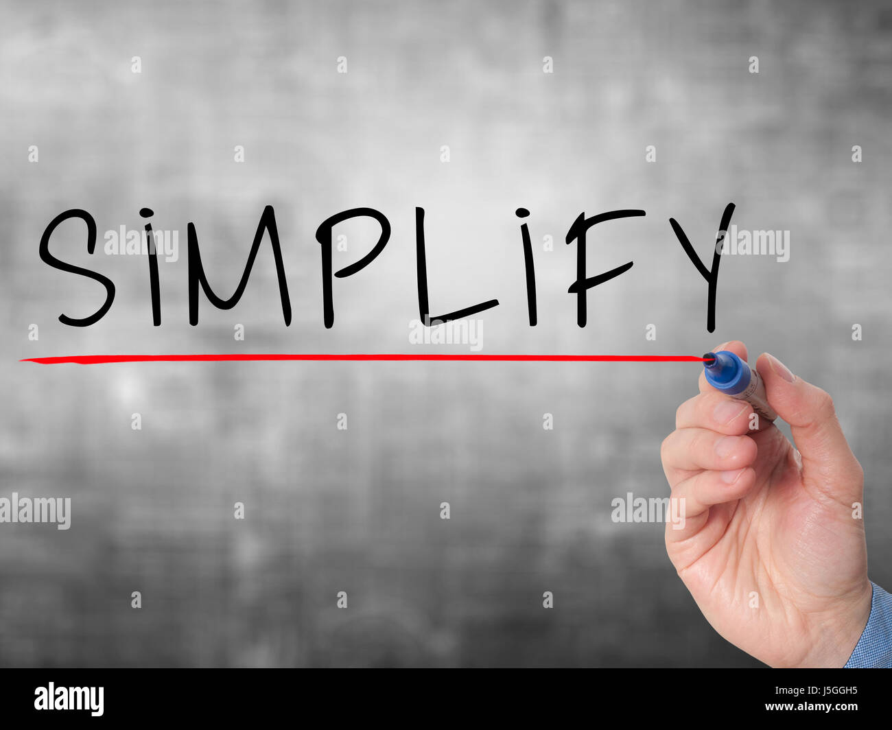Businessman hand writing Simplify with marker on transparent wipe board ...