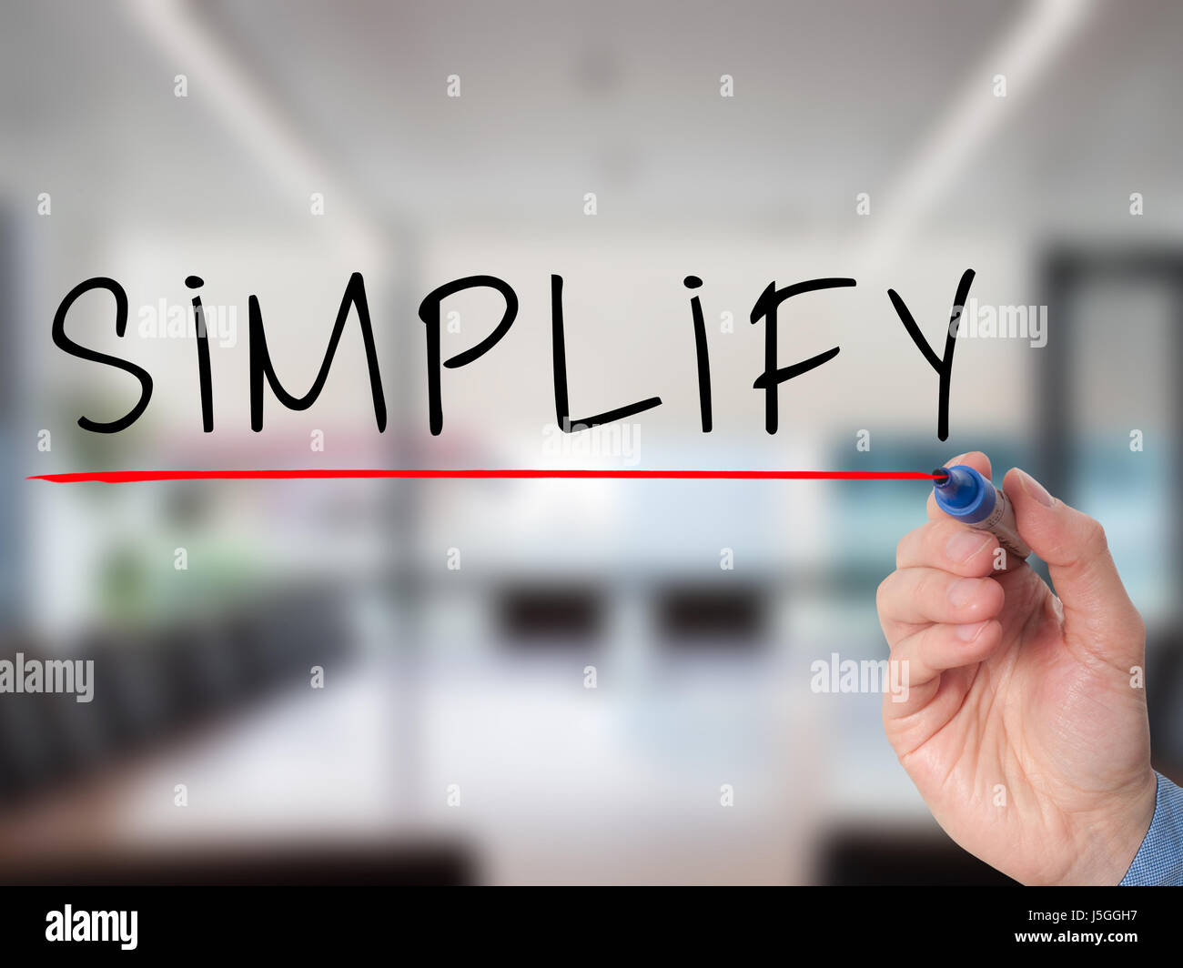 Businessman hand writing Simplify with marker on transparent wipe board ...