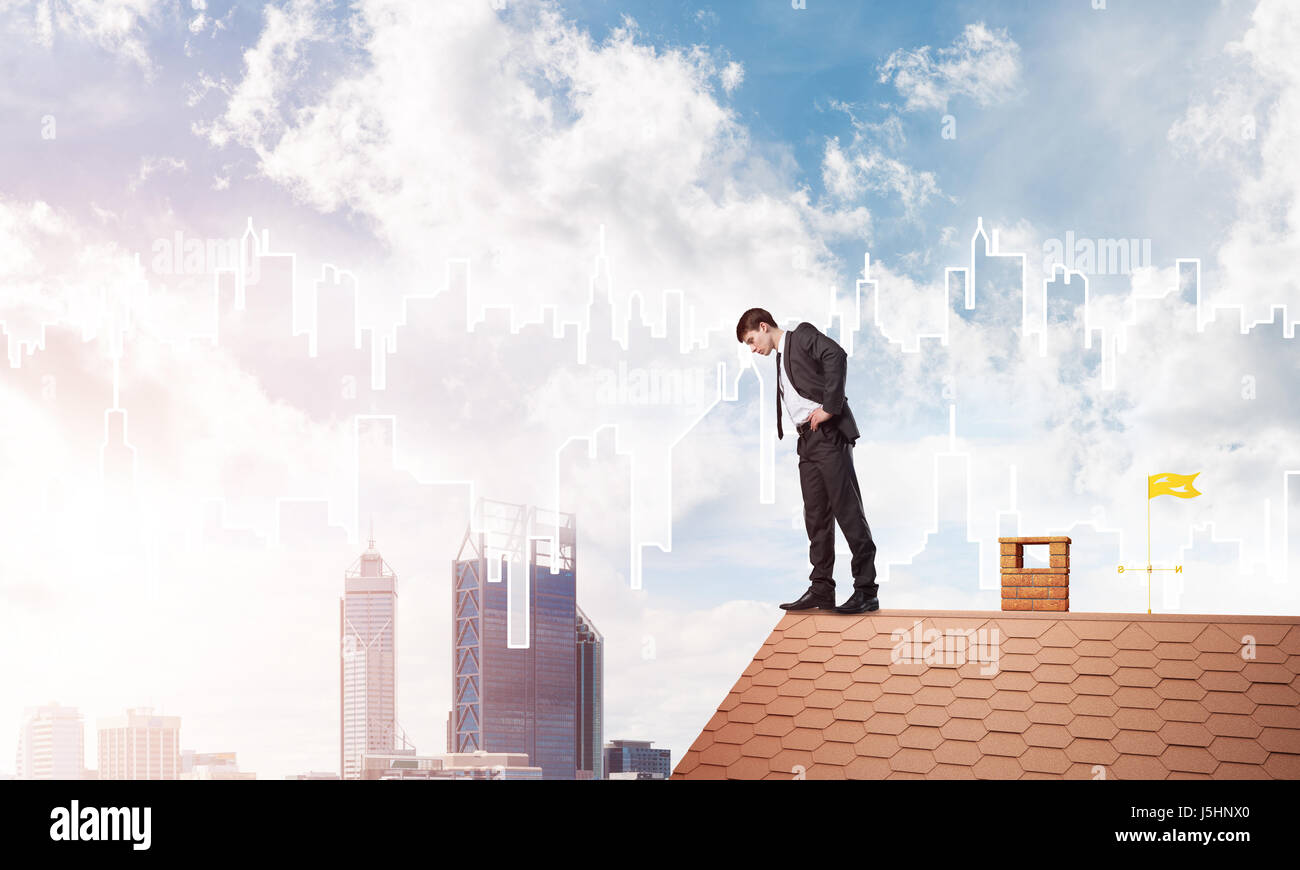 Businessman looking down from roof and modern cityscape at background ...