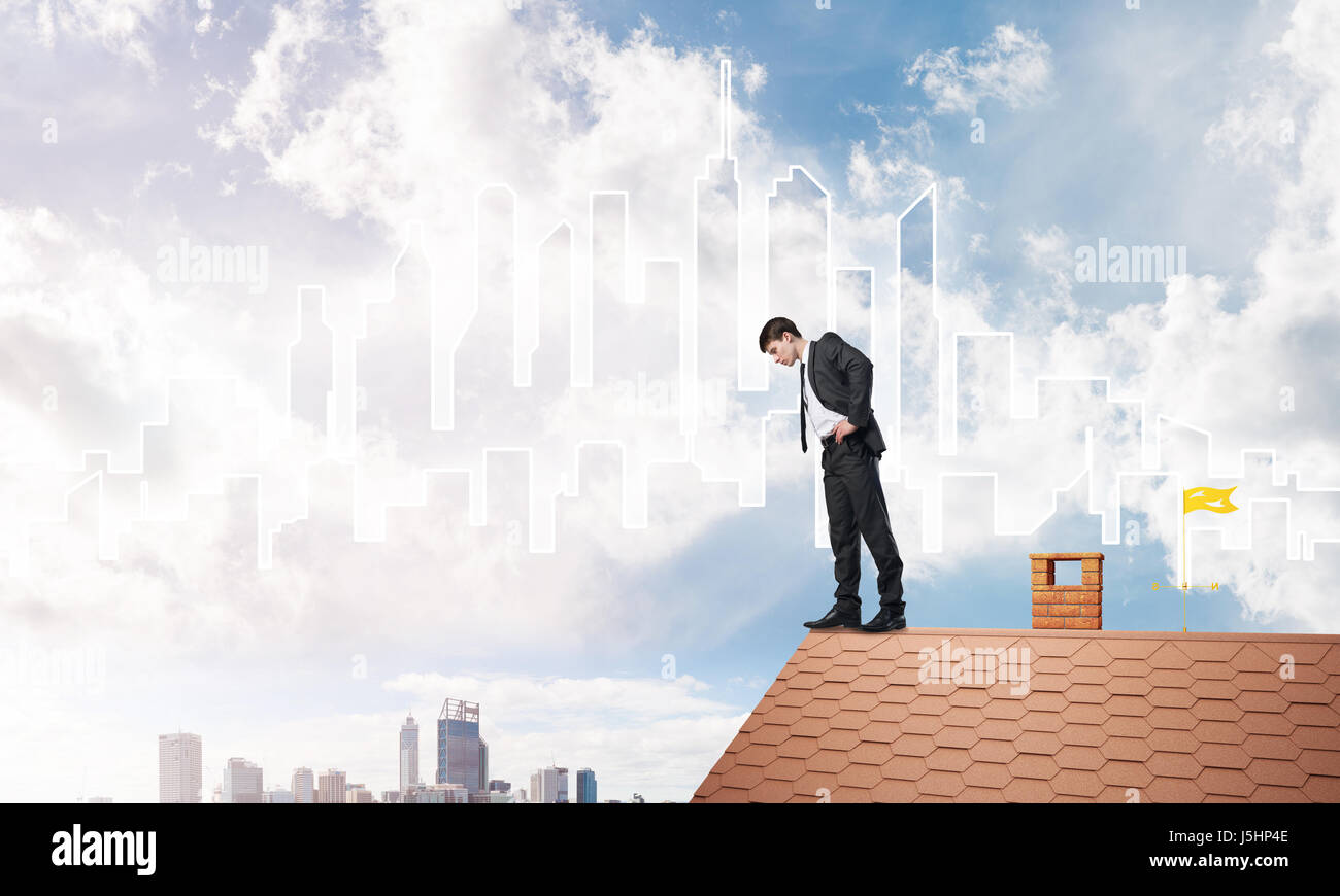 Businessman looking down from roof and modern cityscape at background ...