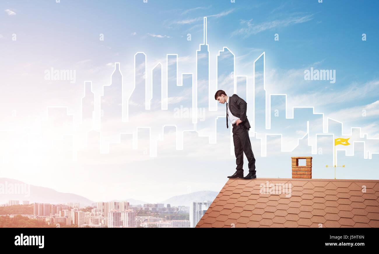Businessman looking down from roof and modern cityscape at background ...