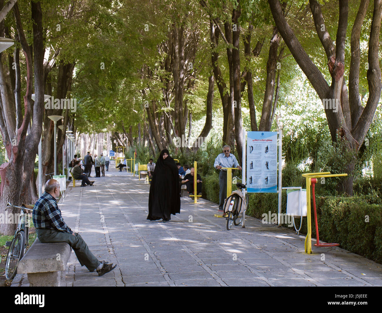 Men and women walk, rest and exercise along shaded Isfahan street, Iran ...