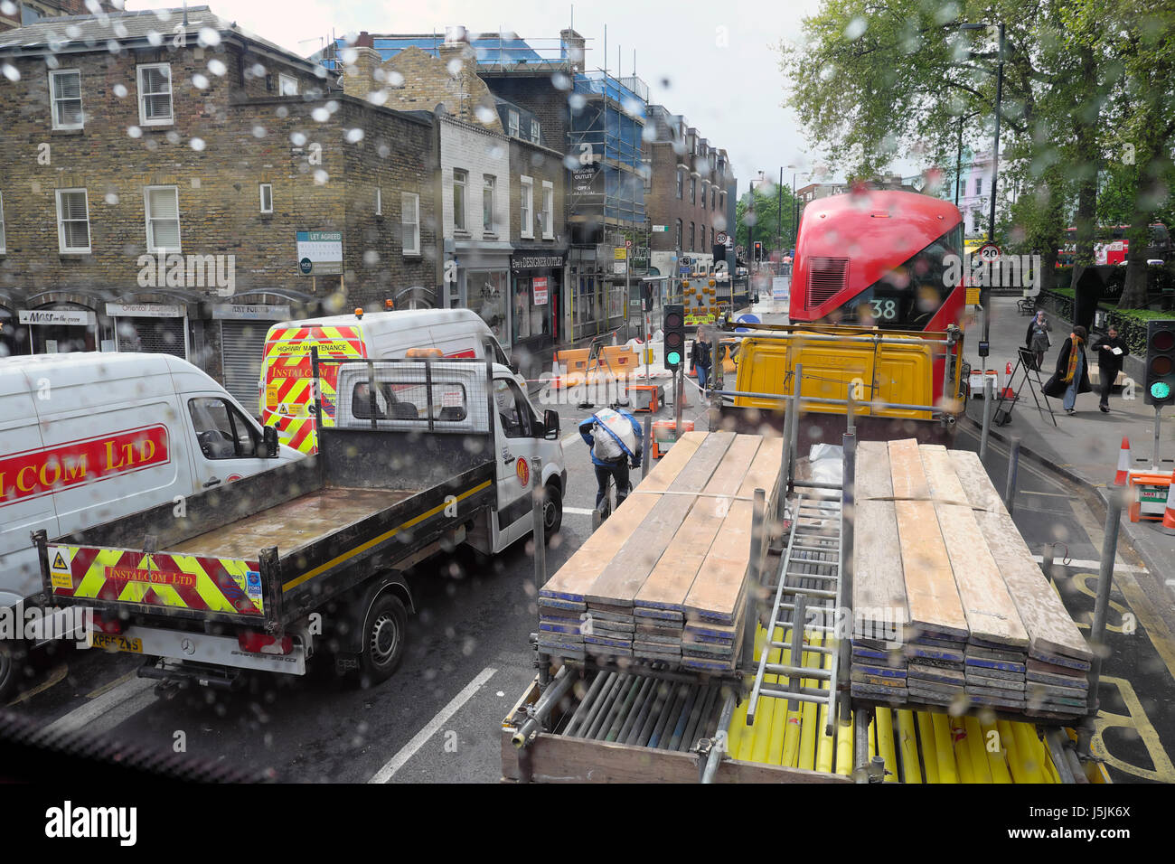 Cyclist cycling between construction lorries behind double-decker bus ...
