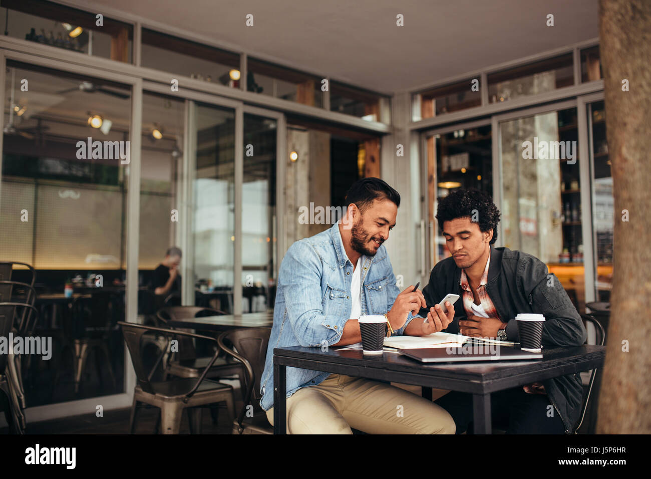 Two young men sitting together at coffee shop using mobile phone ...
