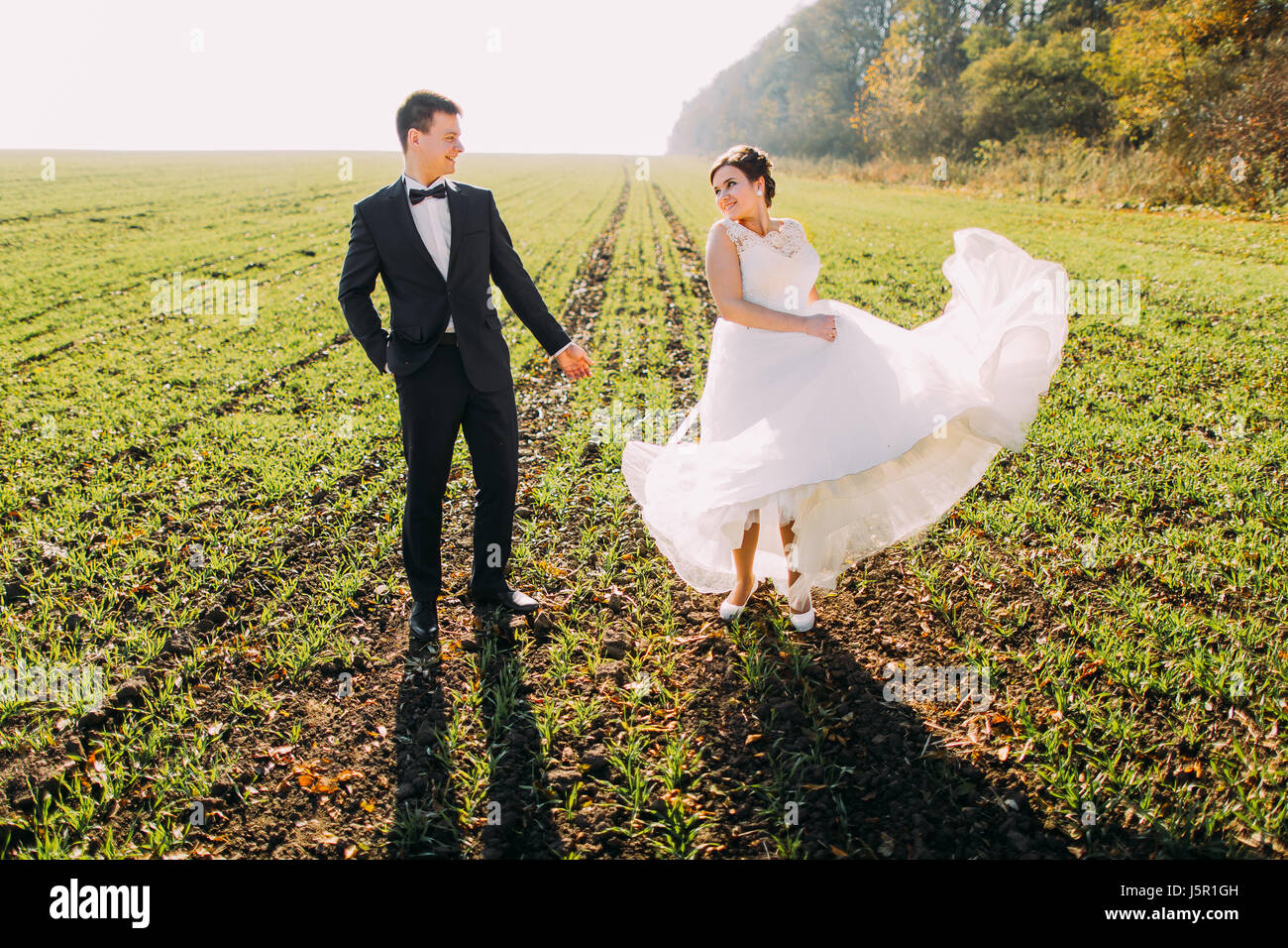 Lovely view of the newlyweds in the green field. The bride is playing ...