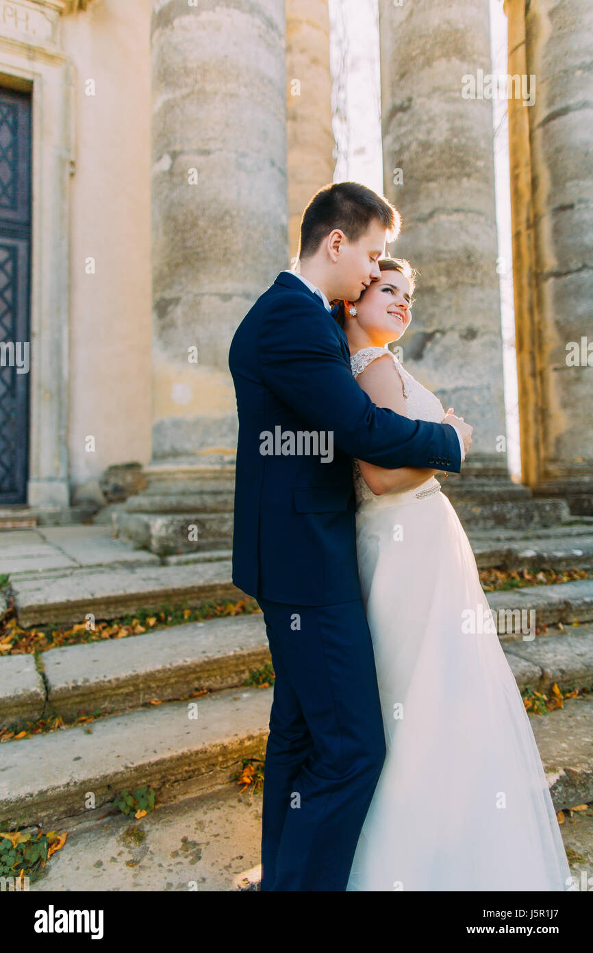 The side view of the groom hugging the bride back while standing on the ...
