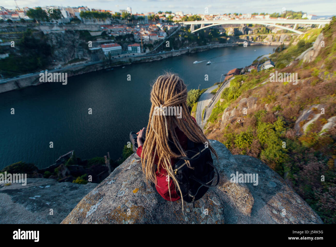 Girl with blonde dreadlocks sitting on a rock and looks at Douro river ...