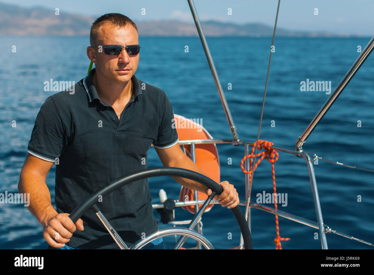 Tanned young male skipper at the helm of a sailing yacht Stock Photo ...