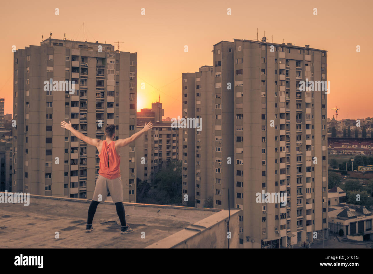 One young adult man only, athlete proud successful, standing on rooftop ...