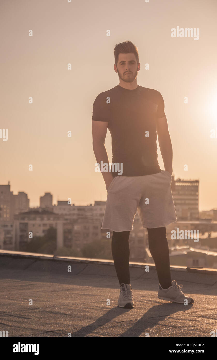 Man standing on rooftop, buildings, sunny Sun, sport clothes, sunset ...