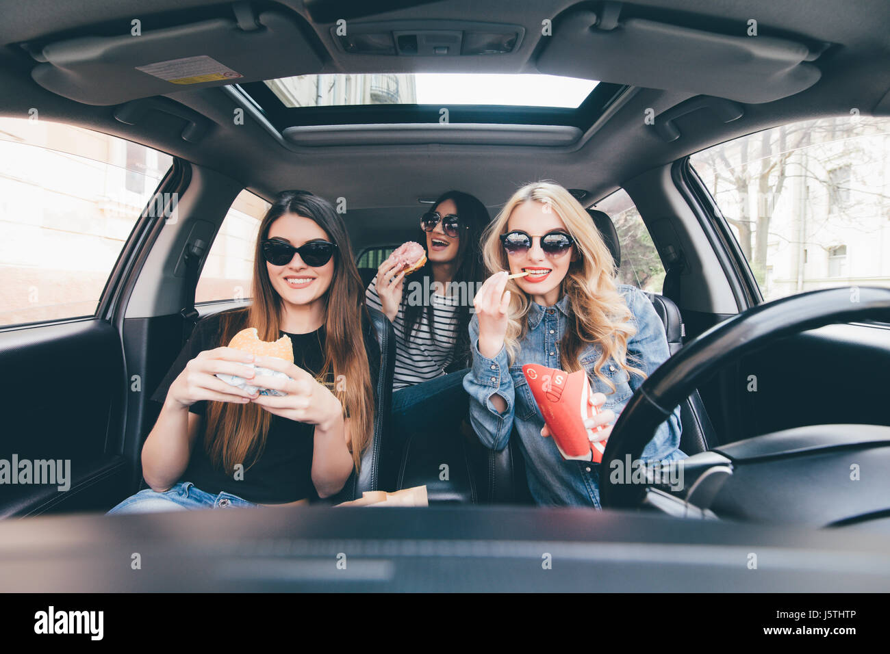 Three young and beauty women have fun together eating fast food and ...