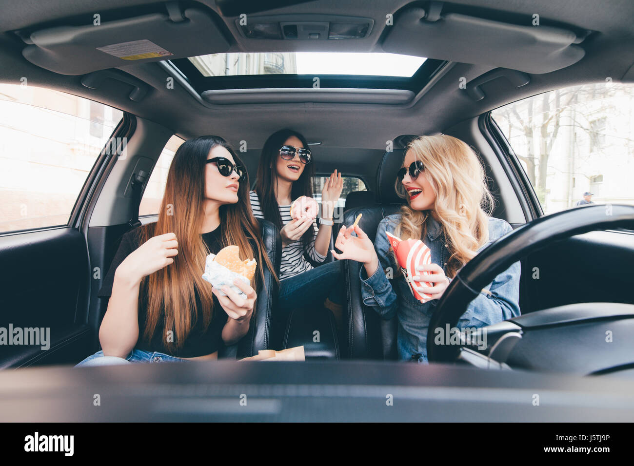 Three young and beauty women have fun together eating fast food and ...