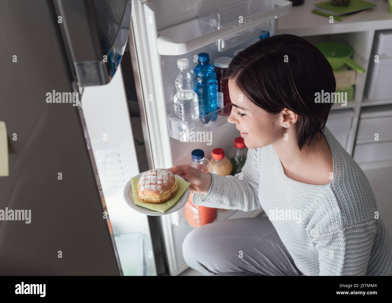 Woman having an unhealthy snack, she is taking a delicious pastry out ...