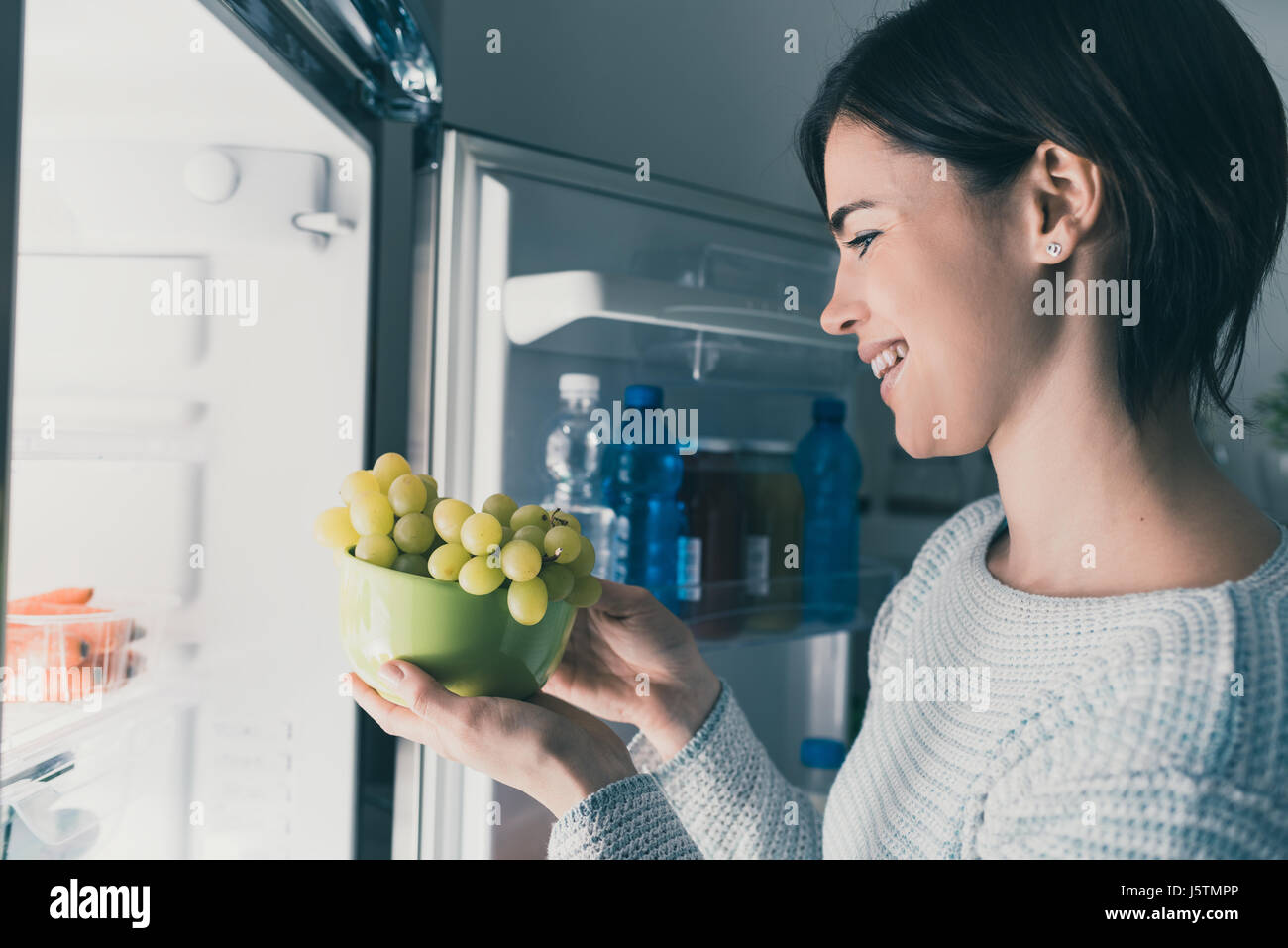 Smiling woman having an healthy snack, she is taking a bowl of fruit ...