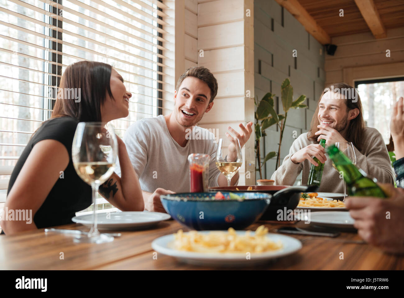 Group of happy young people eating and talking at the table at home ...