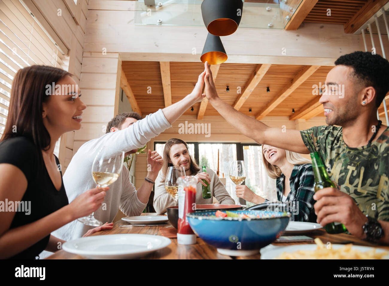 Group of people having dinner and giving high five at the table at home ...
